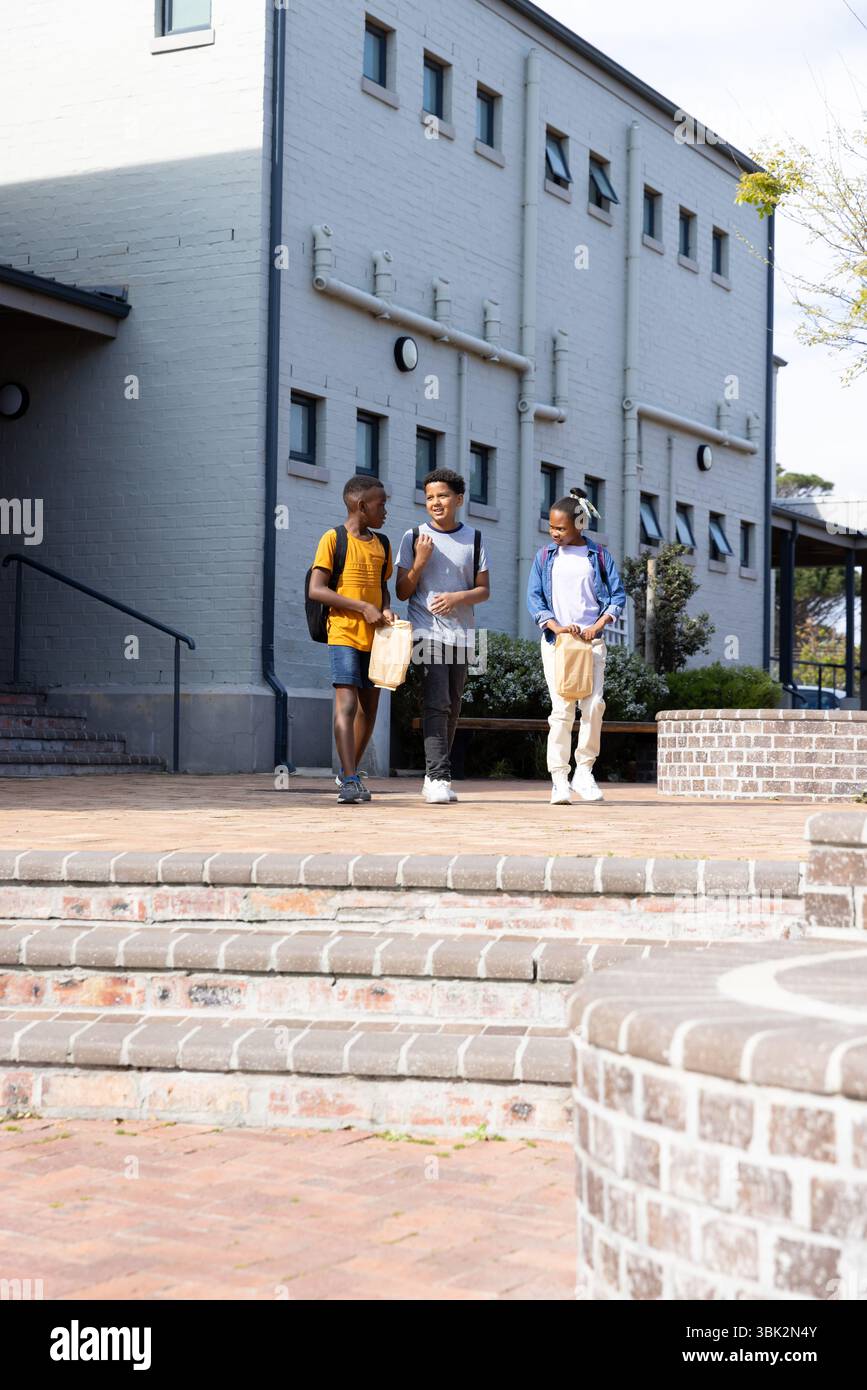 Diverse students walking outside school building, chatting and carrying ...