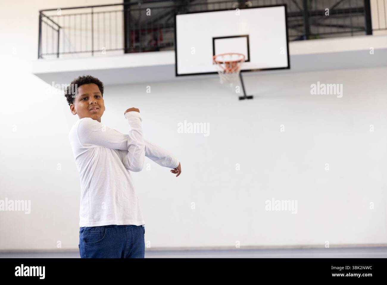 Boy stretching arms in school gym, preparing for basketball practice ...