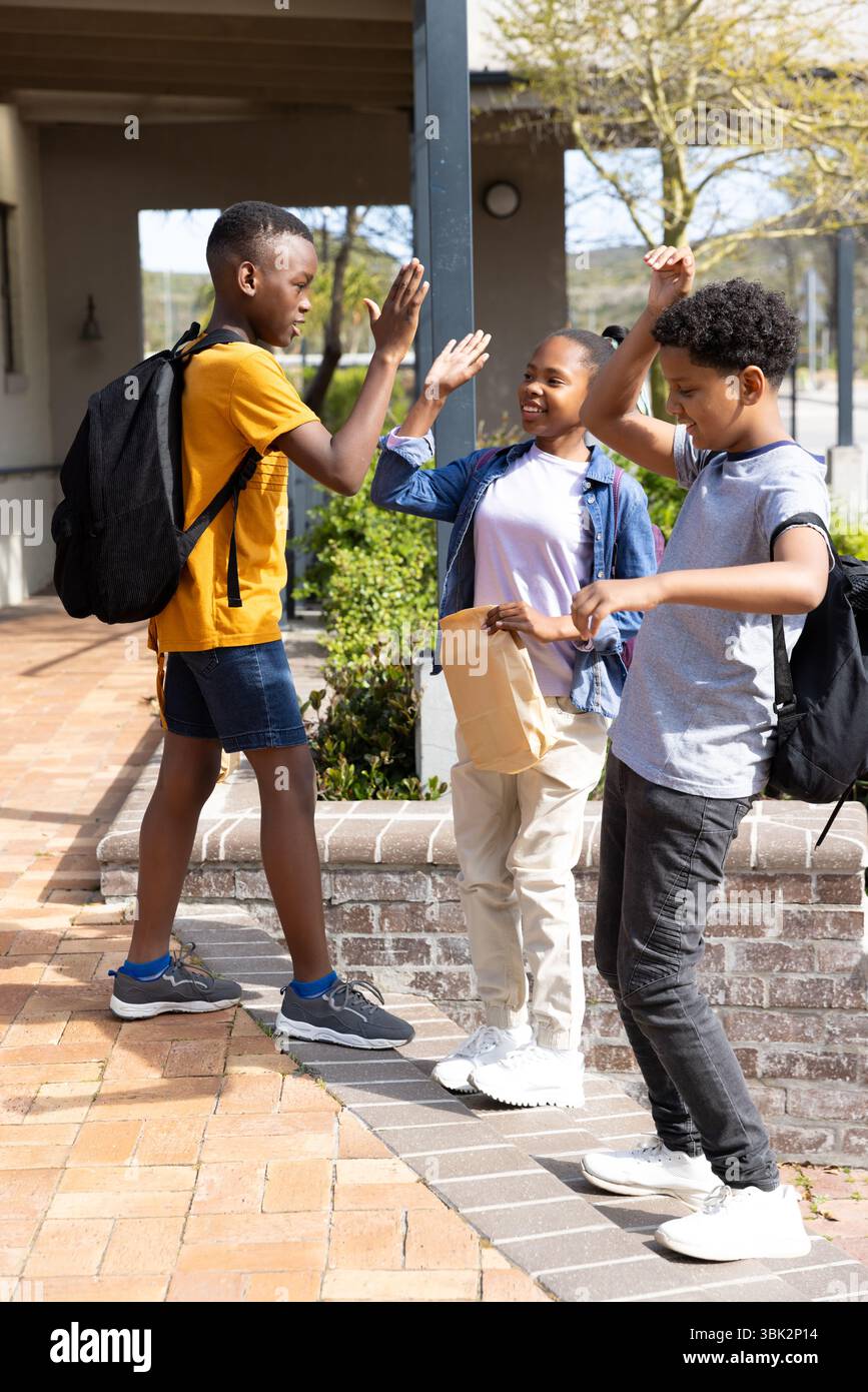 School diverse friends high-fiving and laughing outside, enjoying sunny ...