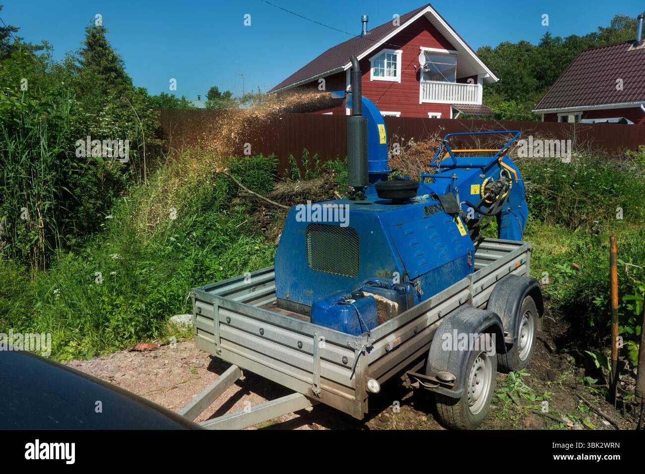 Male Arborist using a working wood chipper machine.The tree surgeon is ...