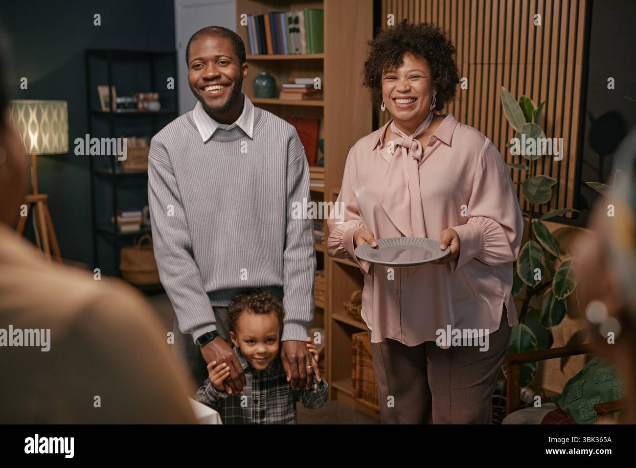 Black couple standing with child and holding plates joyfully ...