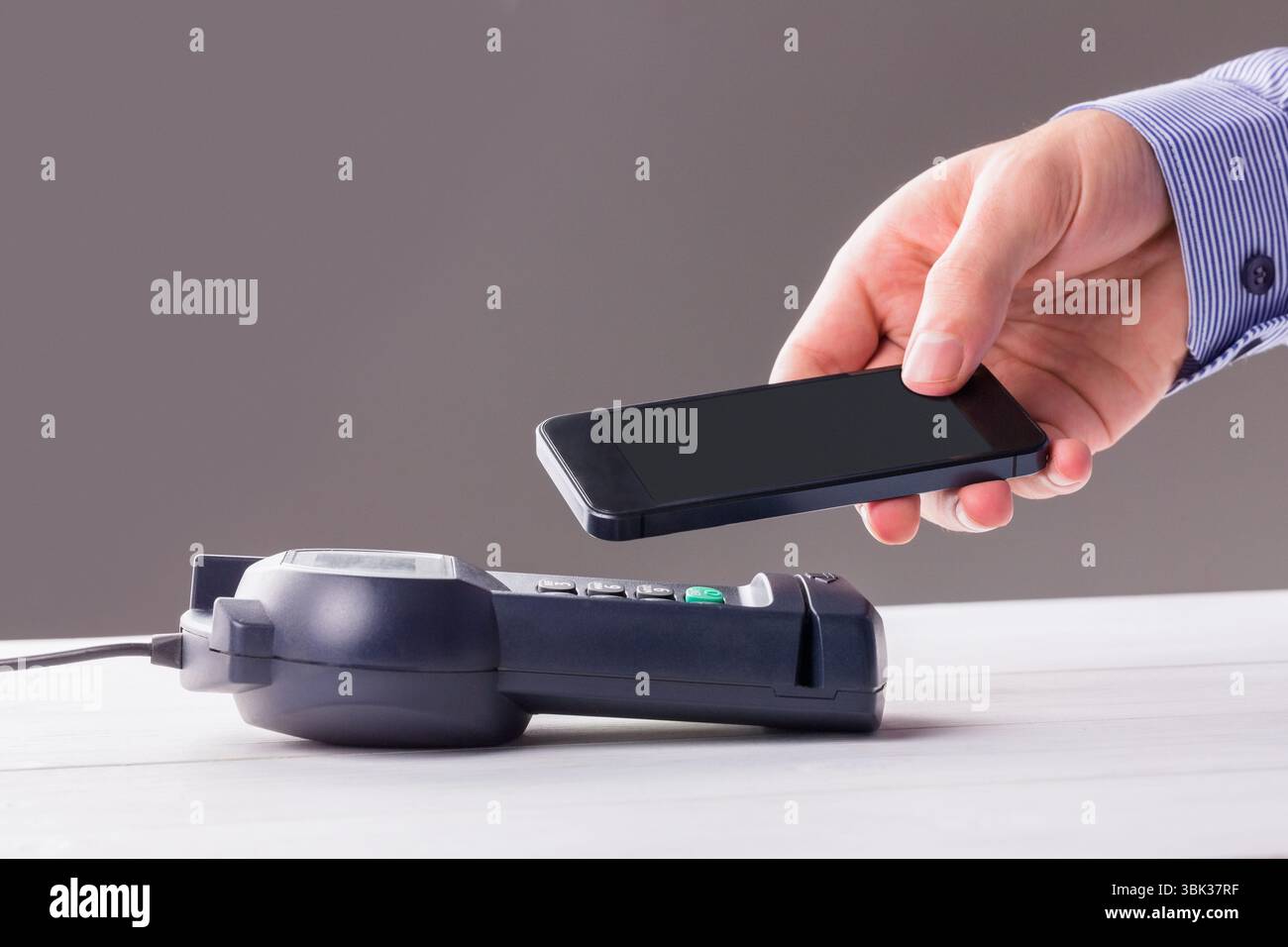 Hand holding black smartphone is making contactless payment over gray ...