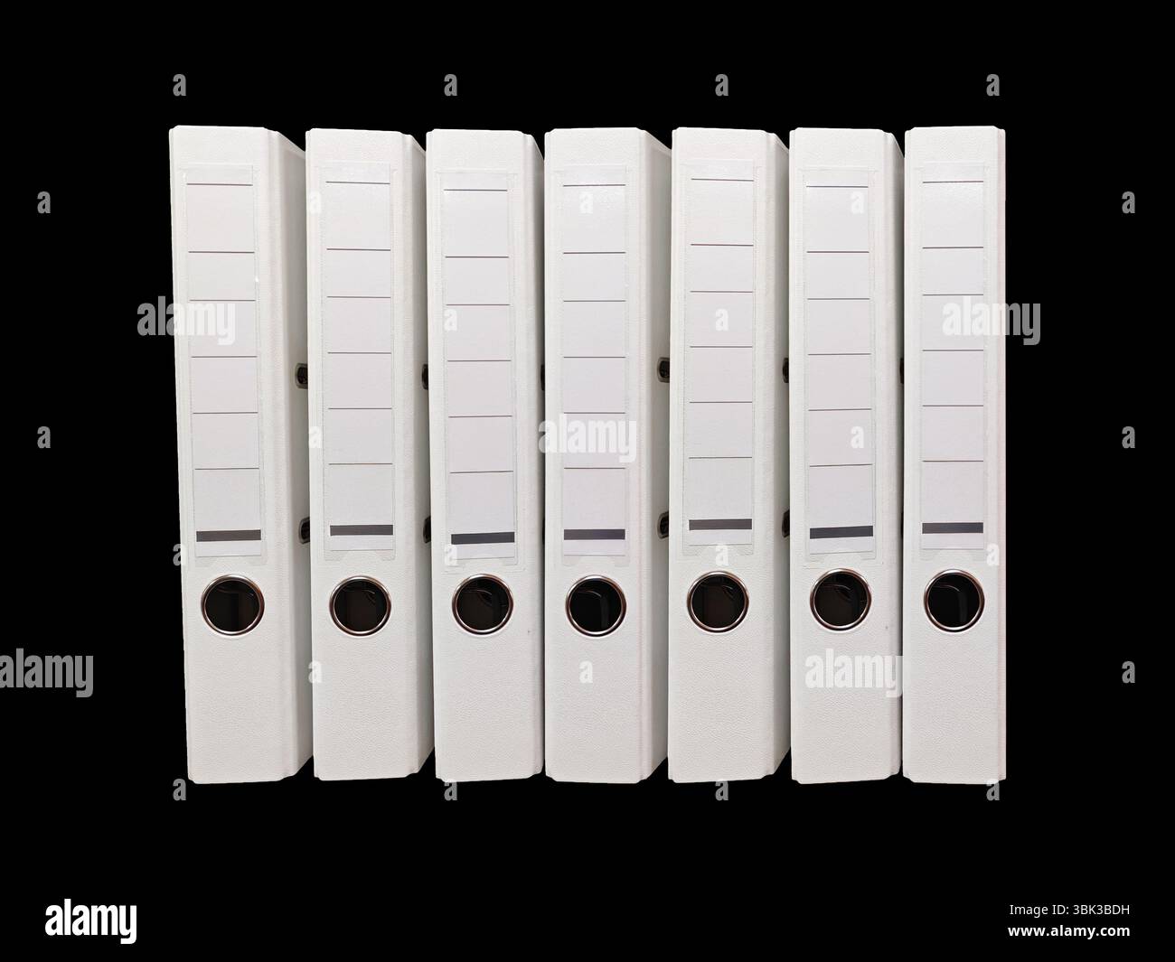 Seven white binders lined up against a black backdrop create a ...