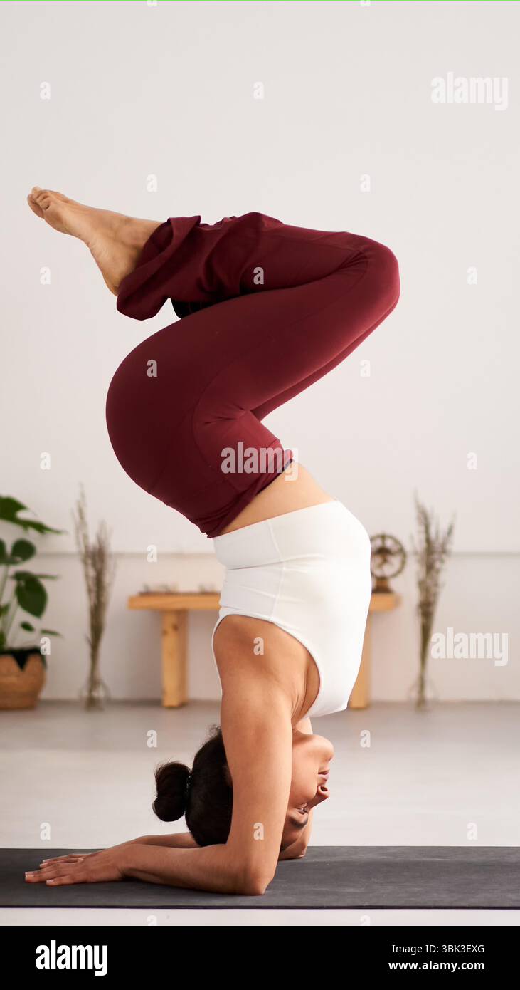 Young woman practicing supported headstand yoga pose at home studio ...