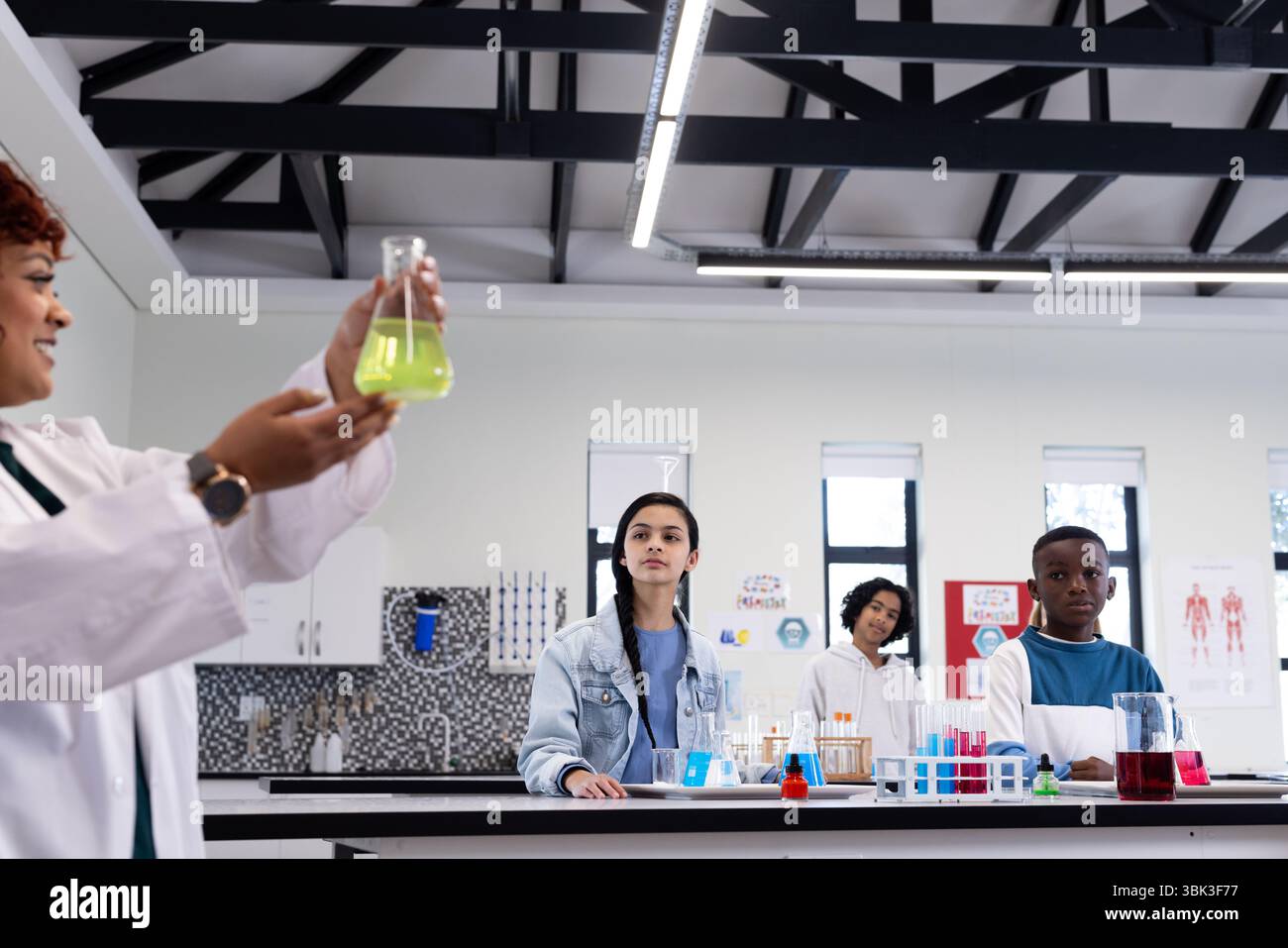 In school, female teacher demonstrating chemistry experiment to diverse ...