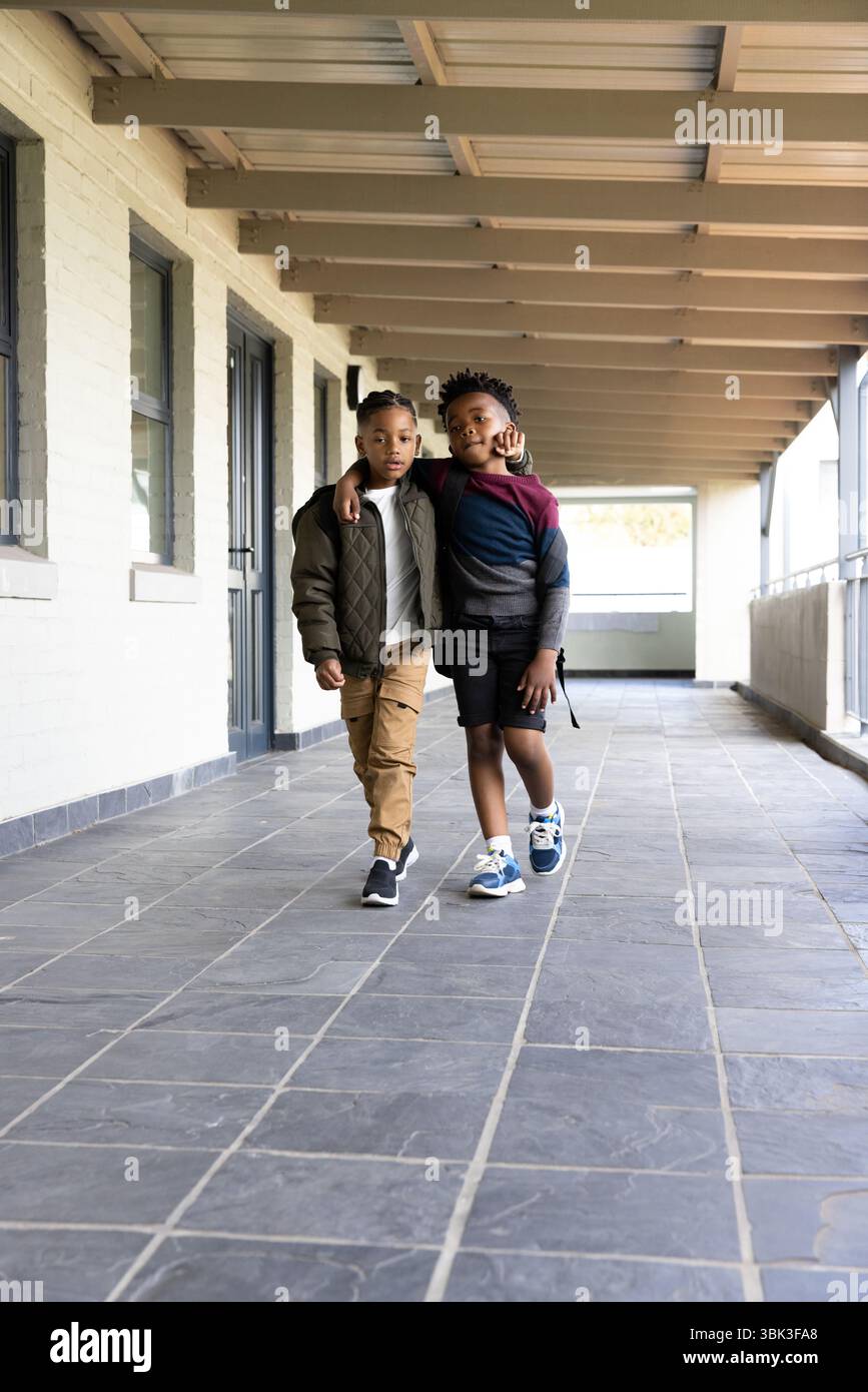Two diverse boys walking arm in arm down school hallway, enjoying ...