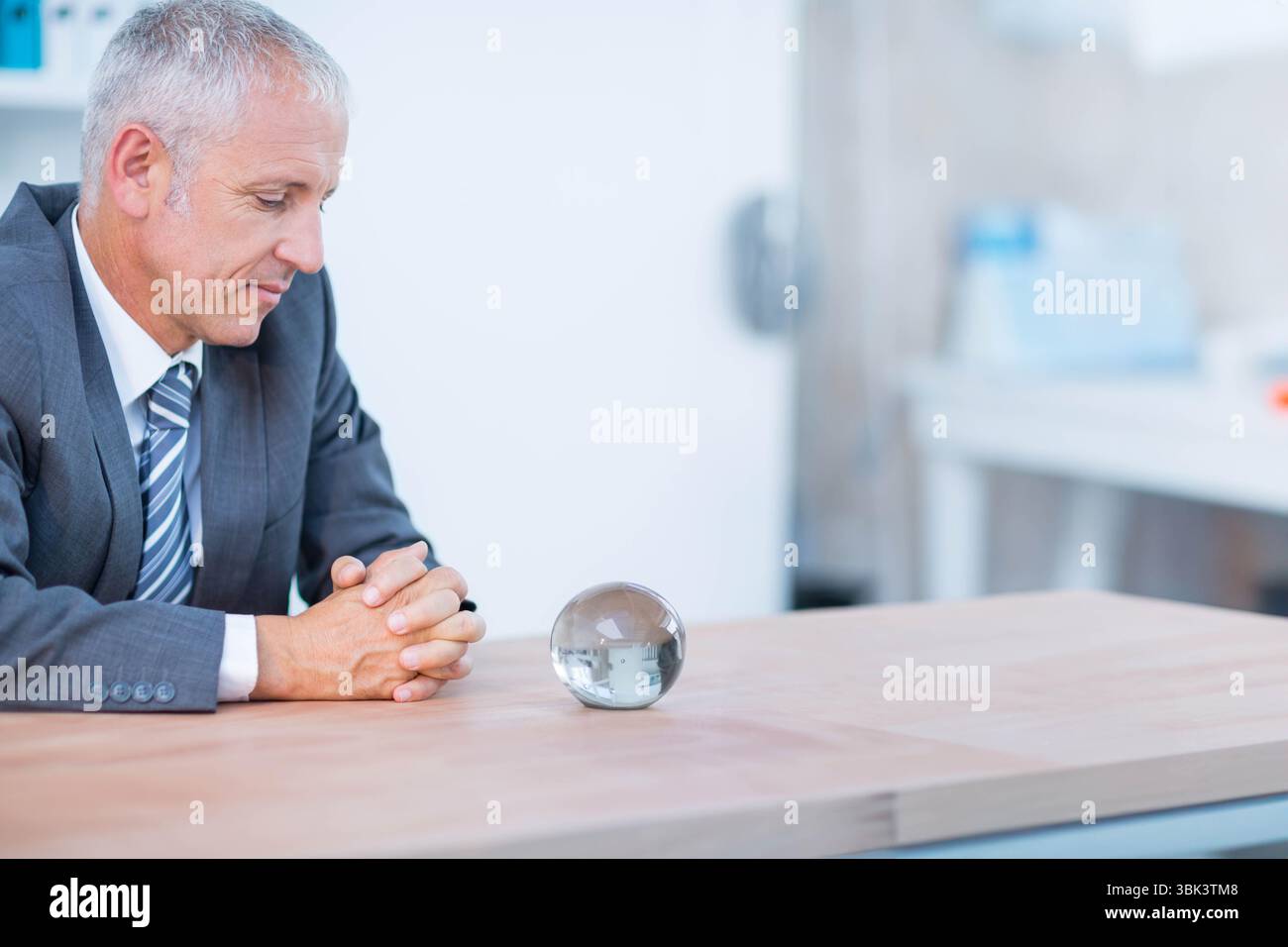 Senior businessman wearing suit sitting behind desk focusing on crystal ...
