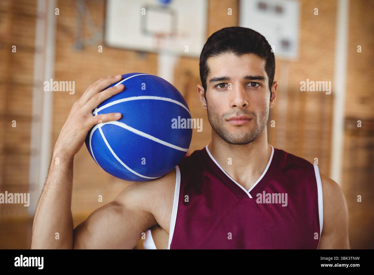 Male basketball player in jersey holding blue basketball on shoulder ...