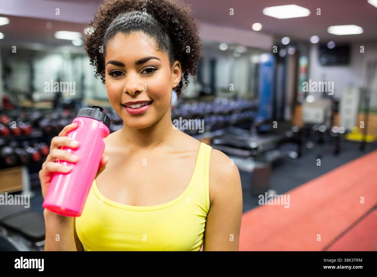 African American woman holding pink shaker bottle standing in gym ...