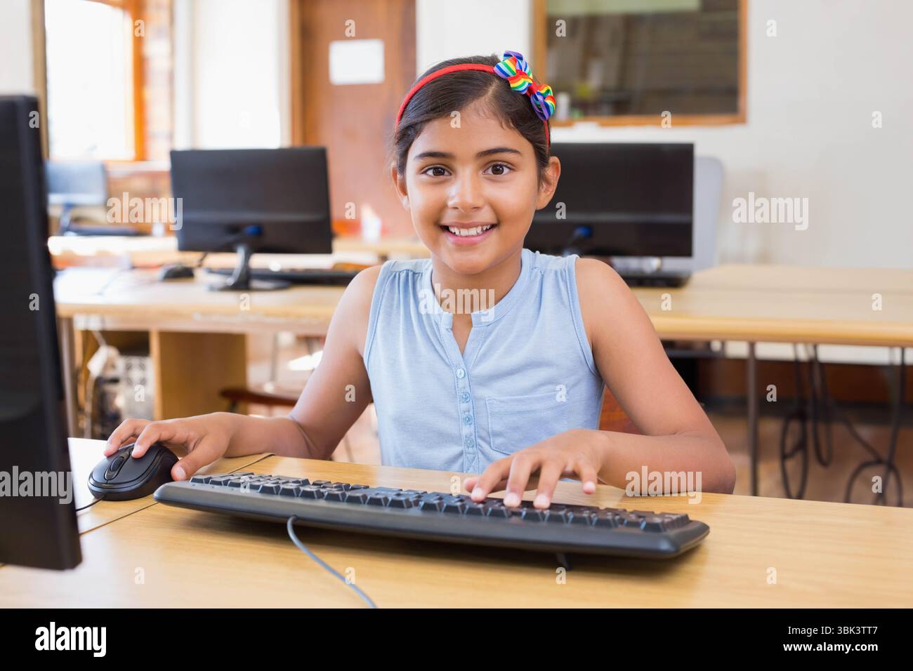 Indian schoolgirl wearing headband smiling at monitor in computer lab ...
