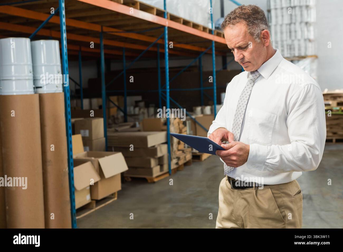 Male warehouse supervisor checking tablet while walking through racks ...