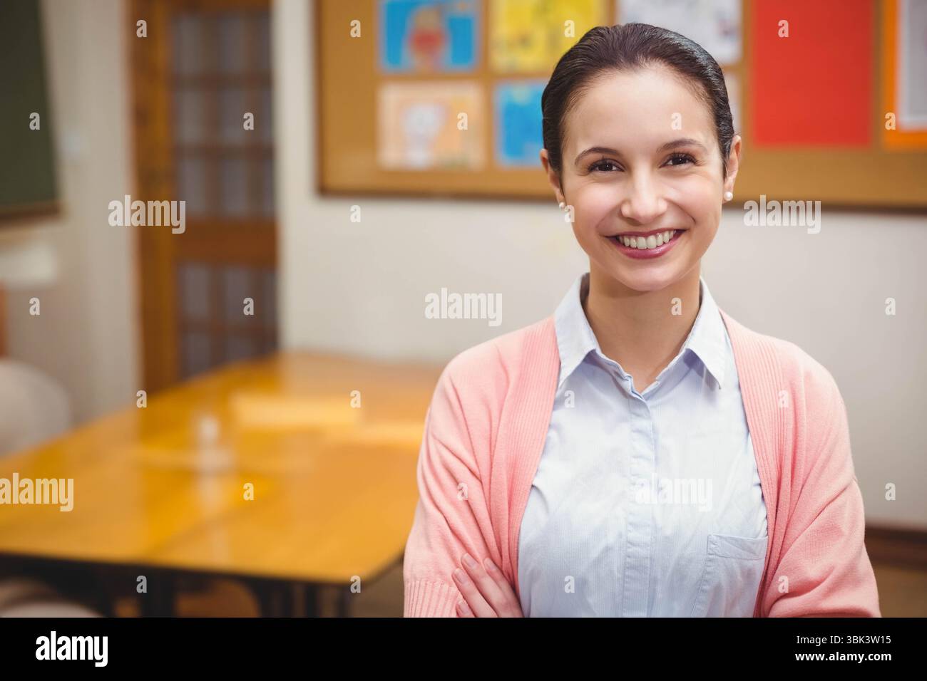Female teacher standing arms folded beside wooden table and chairs in meeting room, copy space ...