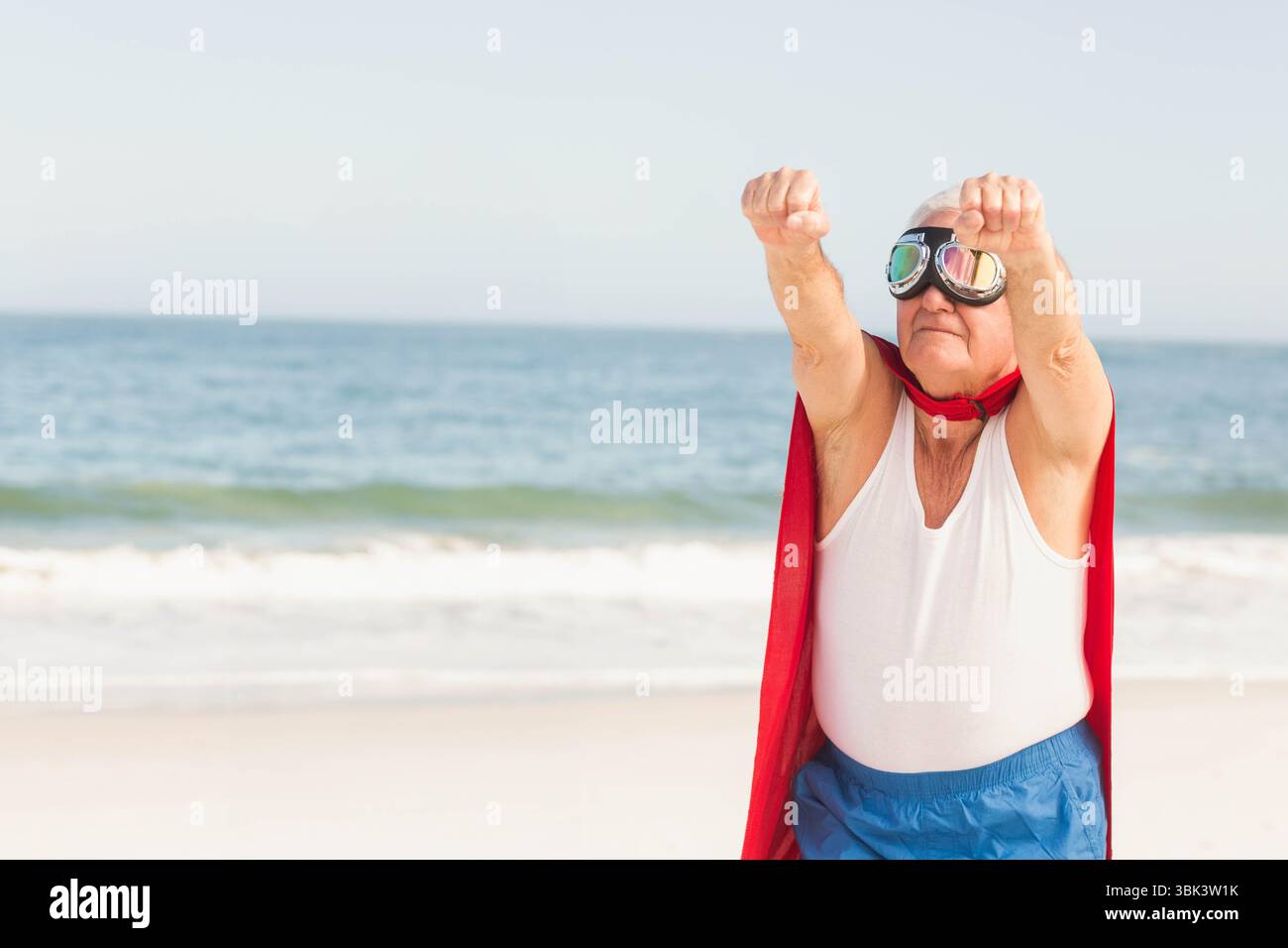 Senior man is standing on sandy shore posing like superhero with red ...