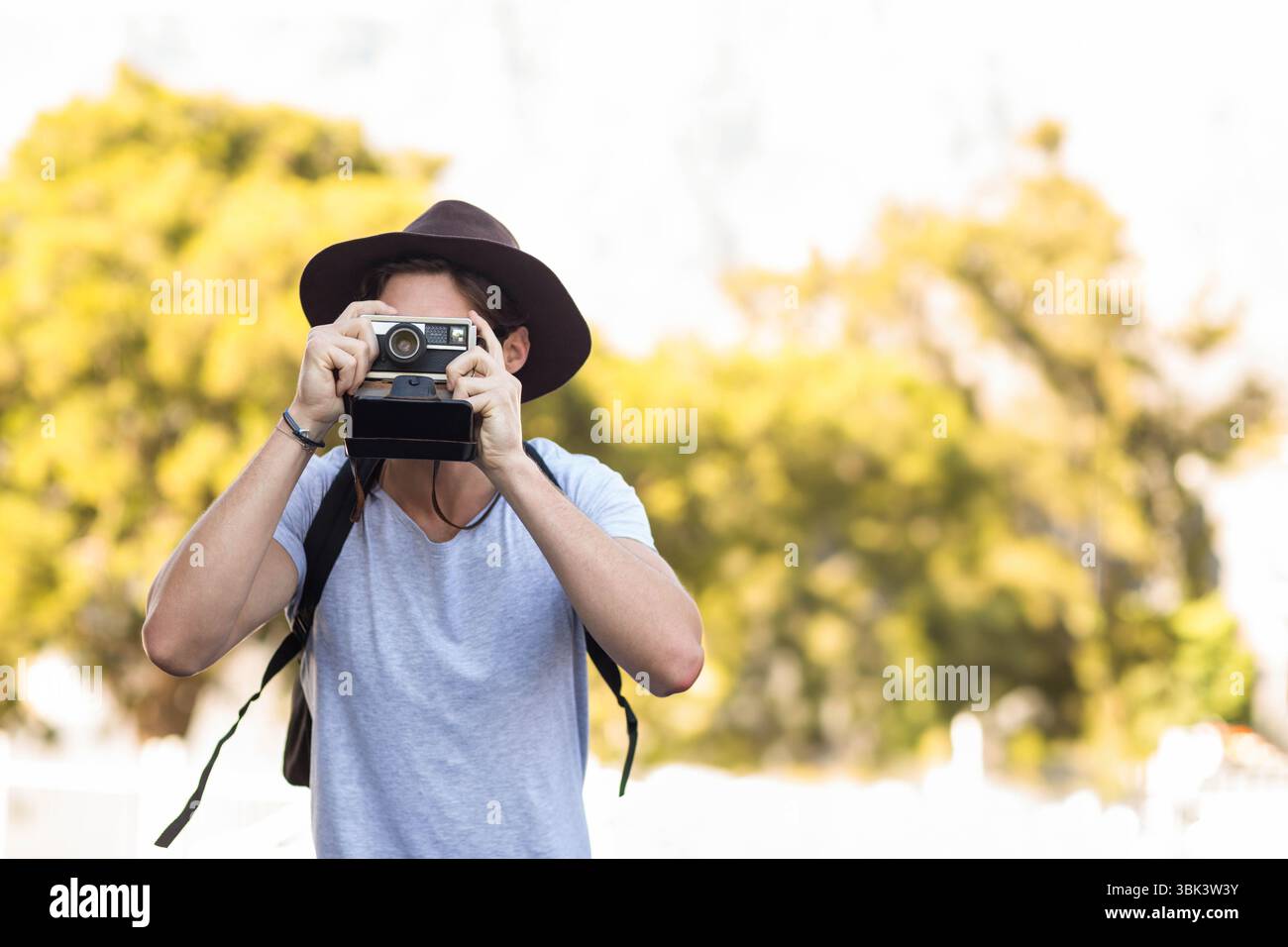 Man holding vintage instant camera, capturing sunlit tree canopy in ...