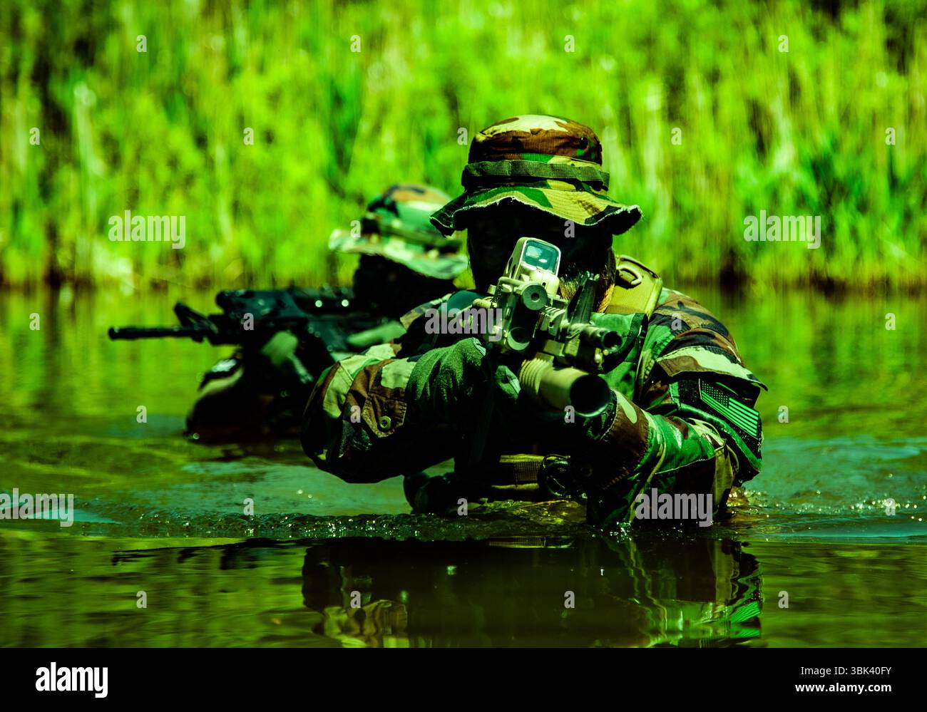 Soldiers in camouflage uniforms with rifles navigate through water in a ...