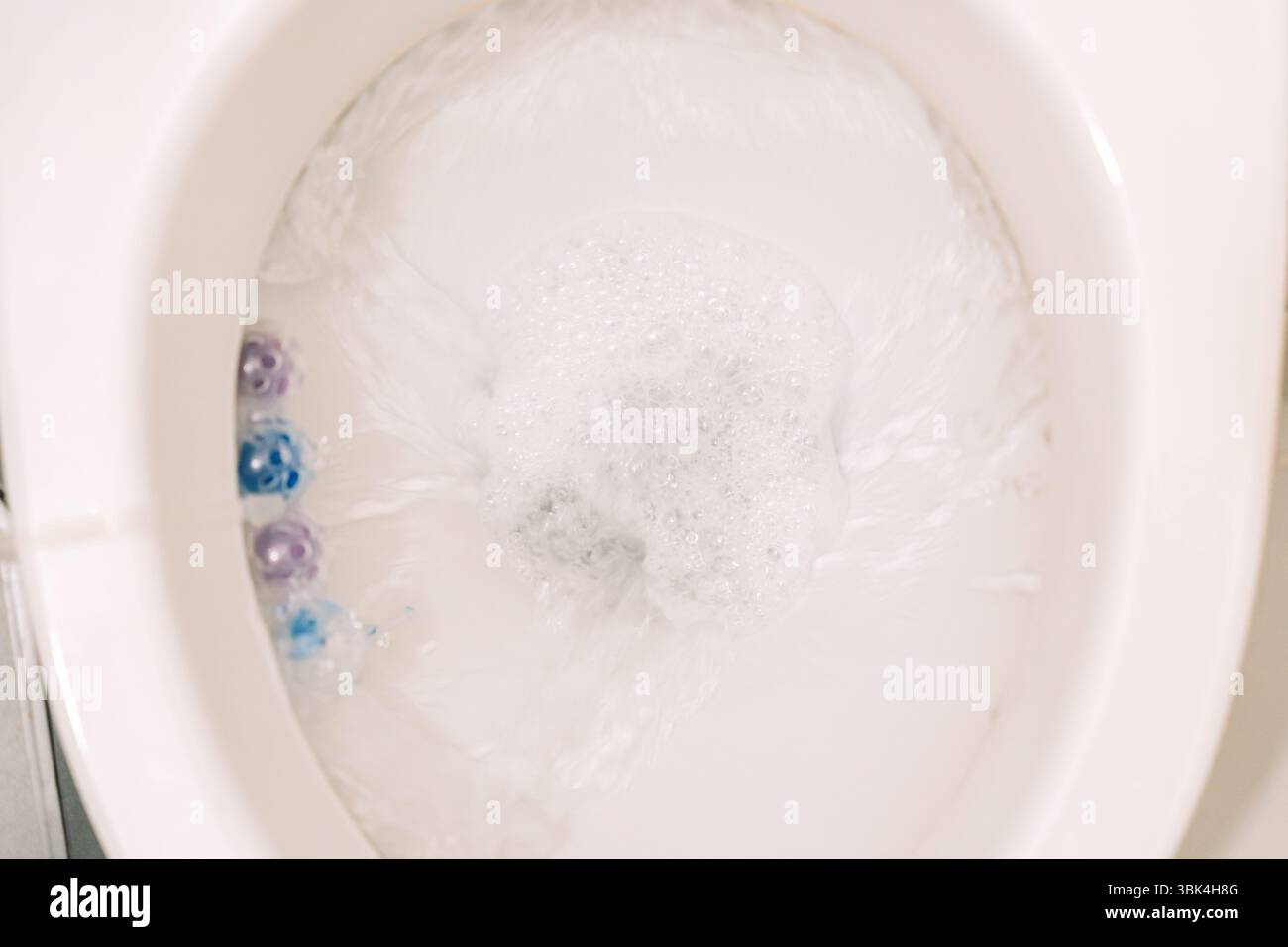 Water swirling in a clean toilet bowl with bubbles and toilet cleaner ...
