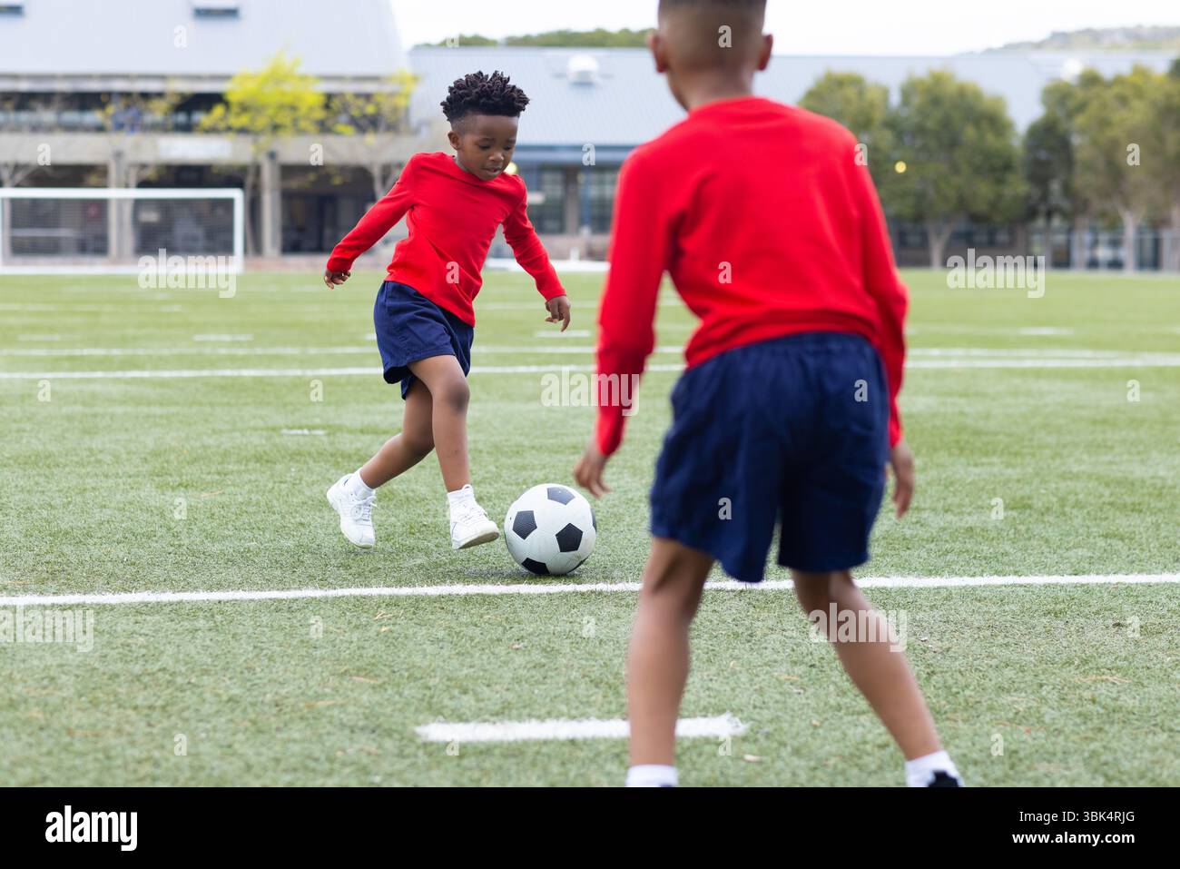 Diverse boys playing soccer on school field, enjoying outdoor activity ...
