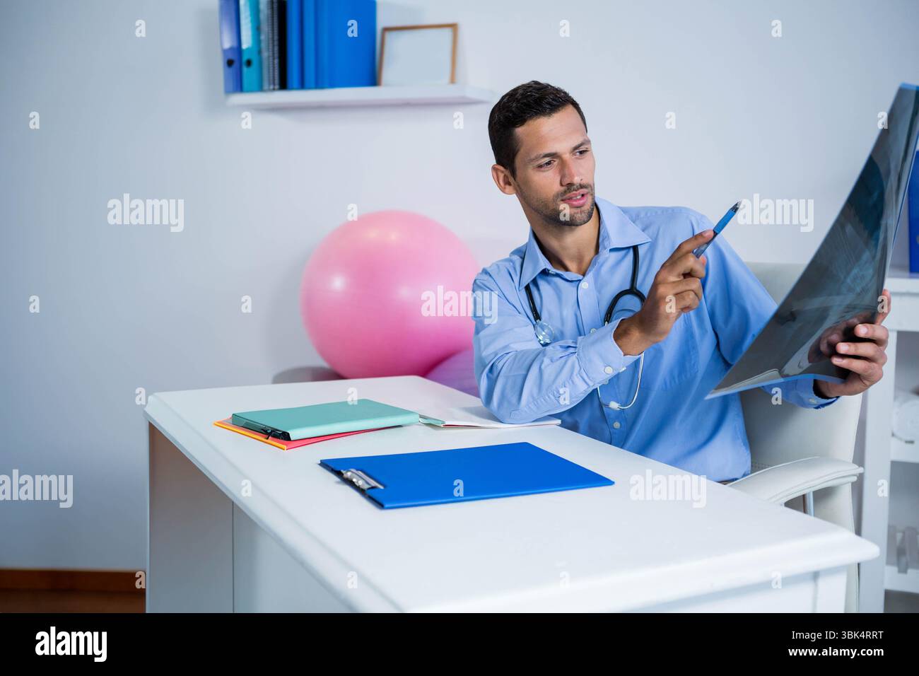 Mid adult male doctor examining X-ray film with stethoscope at desk in ...