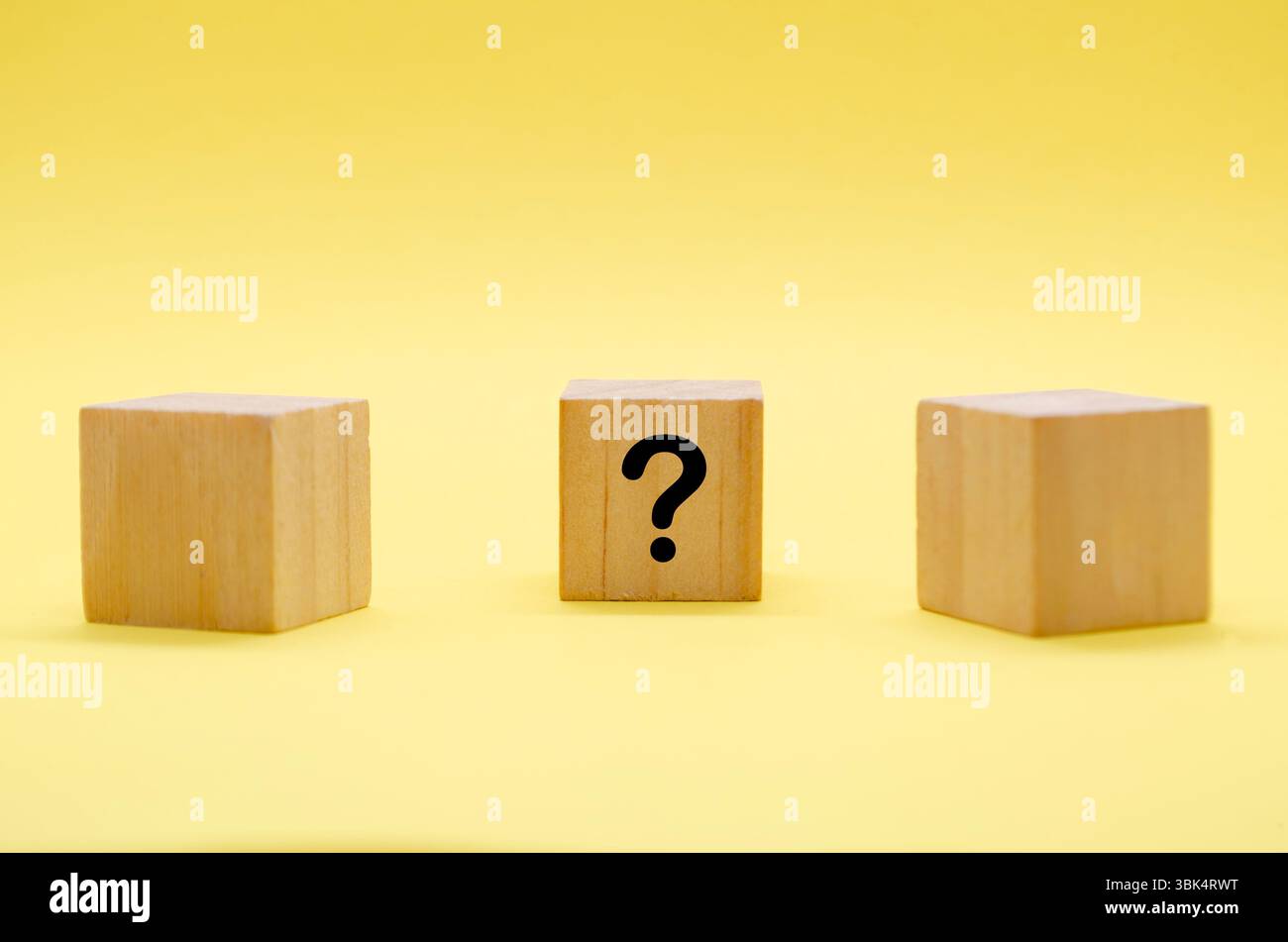 Three light wooden blocks with question marks on pale surface with ...