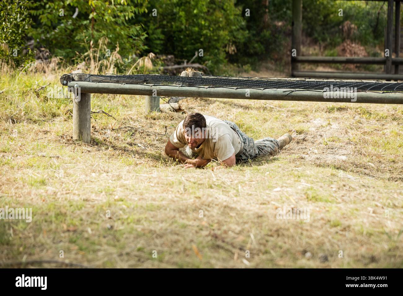 Male soldier wearing camouflage uniform crawling under netted metal ...
