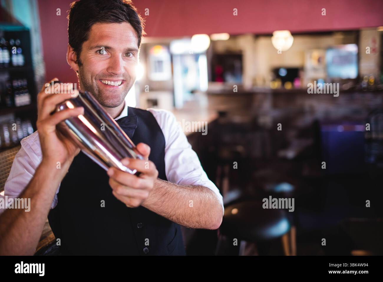 White mid adult male bartender shaking stainless steel cocktail shaker ...