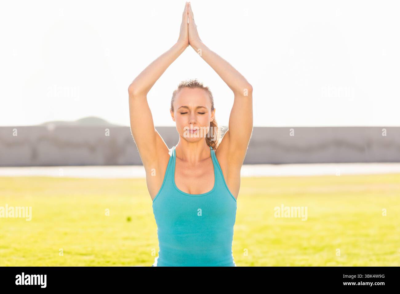 Woman standing on grassy field in yoga prayer pose centering body under ...