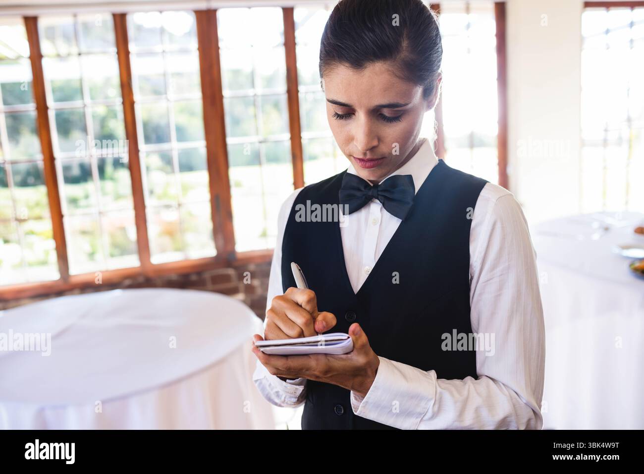 Female server in uniform writing on notepad at banquet hall by white ...