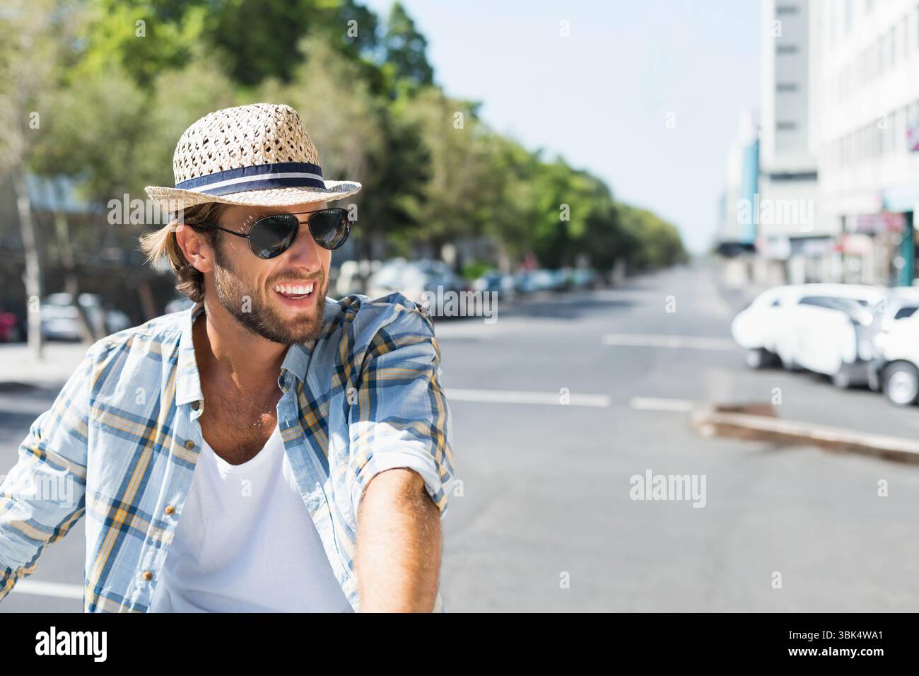Male cyclist wearing straw fedora and sunglasses riding bicycle along ...