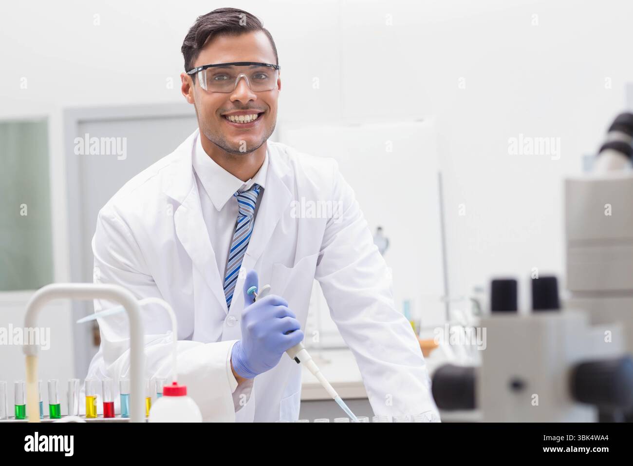 Male scientist in lab coat pipetting liquids into test tube rack with ...