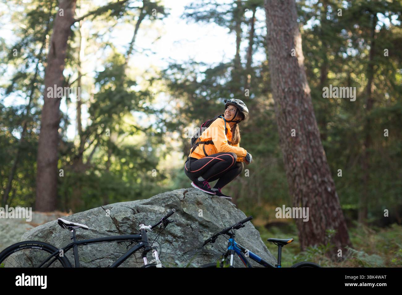 Female cyclist crouching on mossy rock in pine forest adjusting bike ...