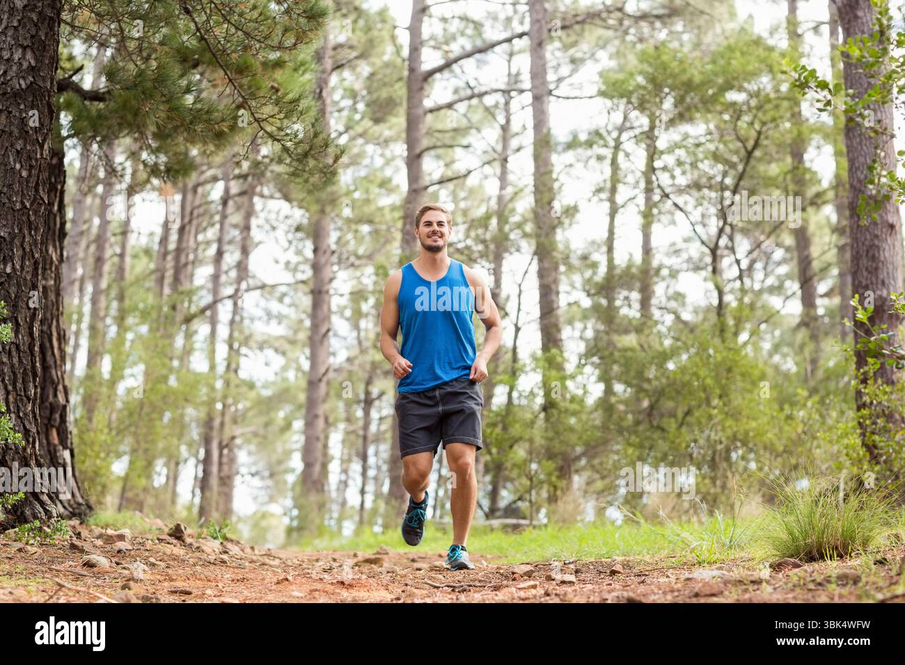 Male runner in blue sportswear jogging along dirt trail through dense ...