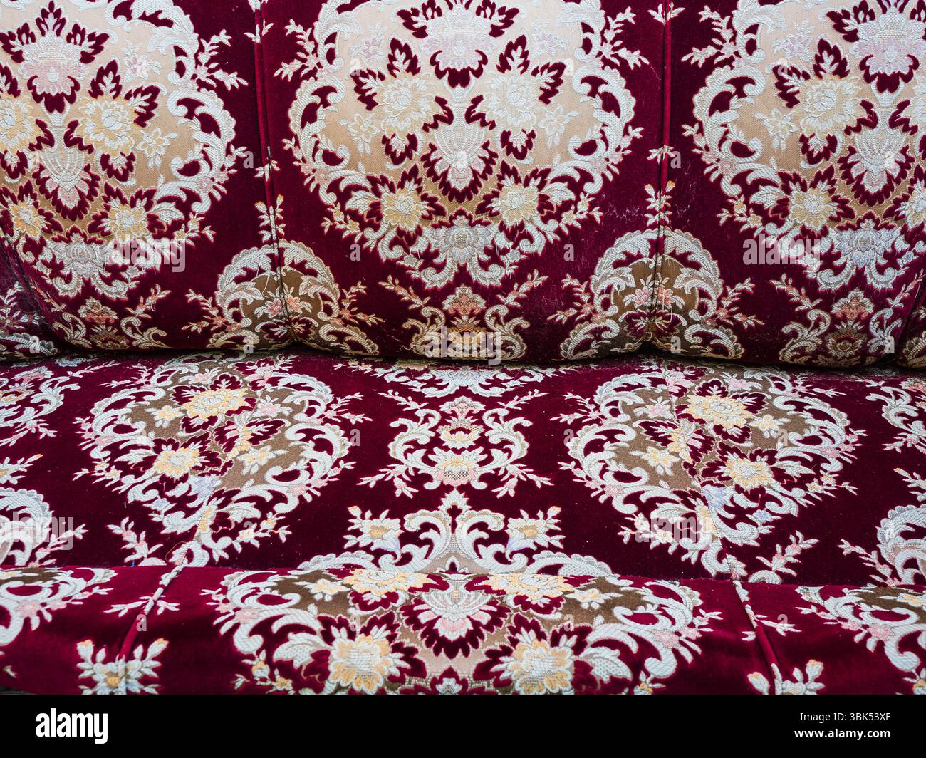 A vintage velvet sofa with intricate patterns in deep red and yellow ...