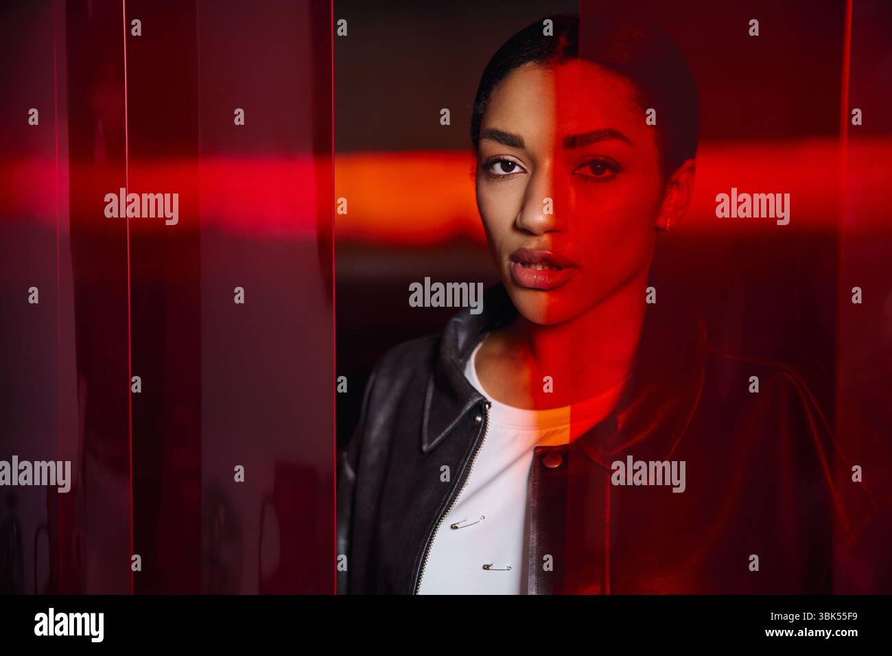 A stylish young woman stands confidently, showcasing her chic attire with striking lighting ...