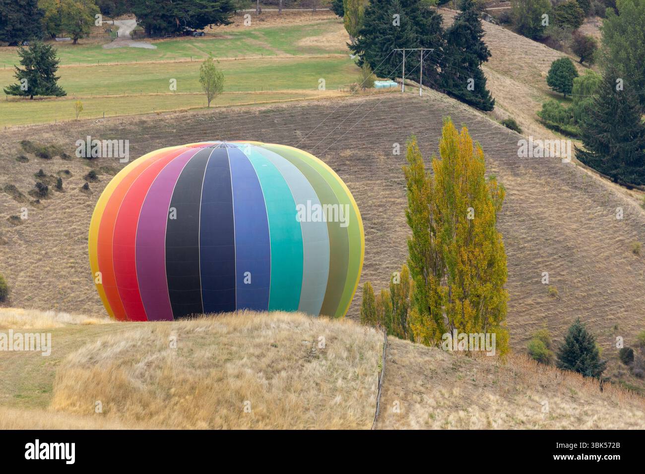 A hot air balloon landing and disappearing between rolling fields near Queenstown, Otago, New ...