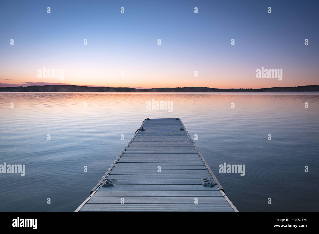Calm lake at sunrise with empty dock leading into still water. Peaceful ...
