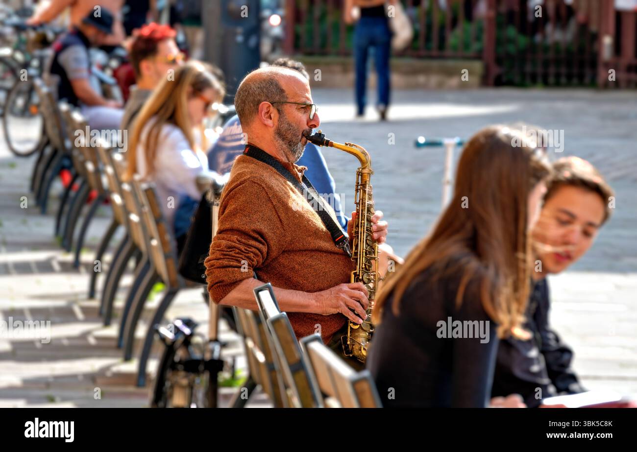 Saxophone musician playing at a square on a chair in sunshine in the ...