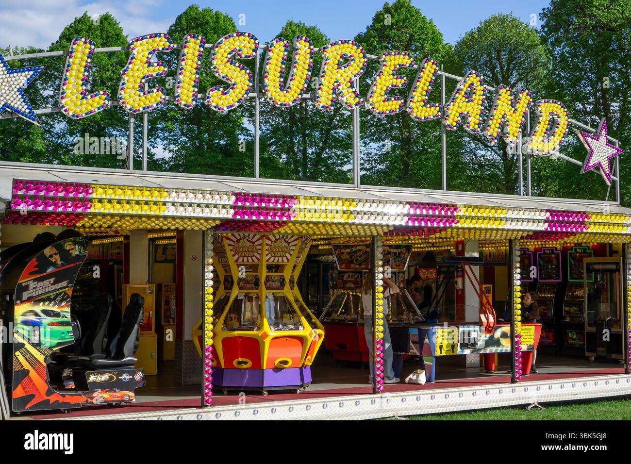 A vibrant funfair scene with the word 'LEISURELAND' brightly lit up, showcasing arcade games and ...