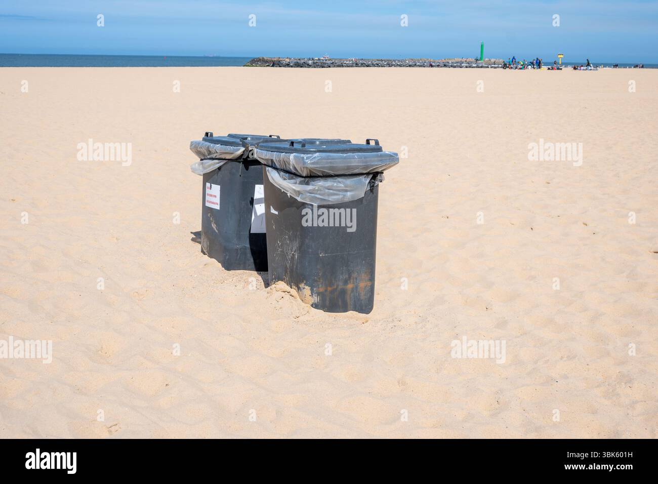 Two black plastic waste containers buried in yellow sand on the beach ...