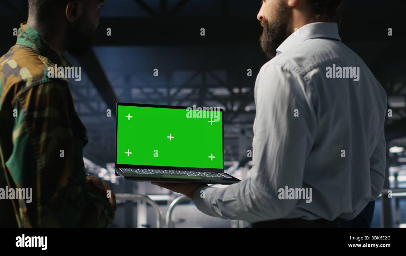 Army tech specialist in data center and coworkers using green screen laptop to troubleshoot ...