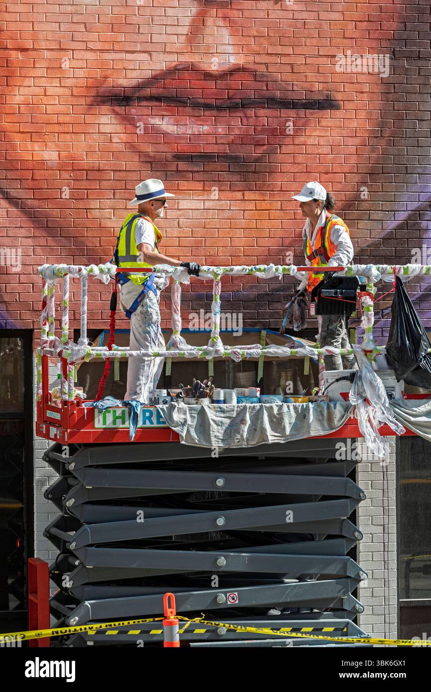 Two artists painting a colorful mural on a brick building while ...