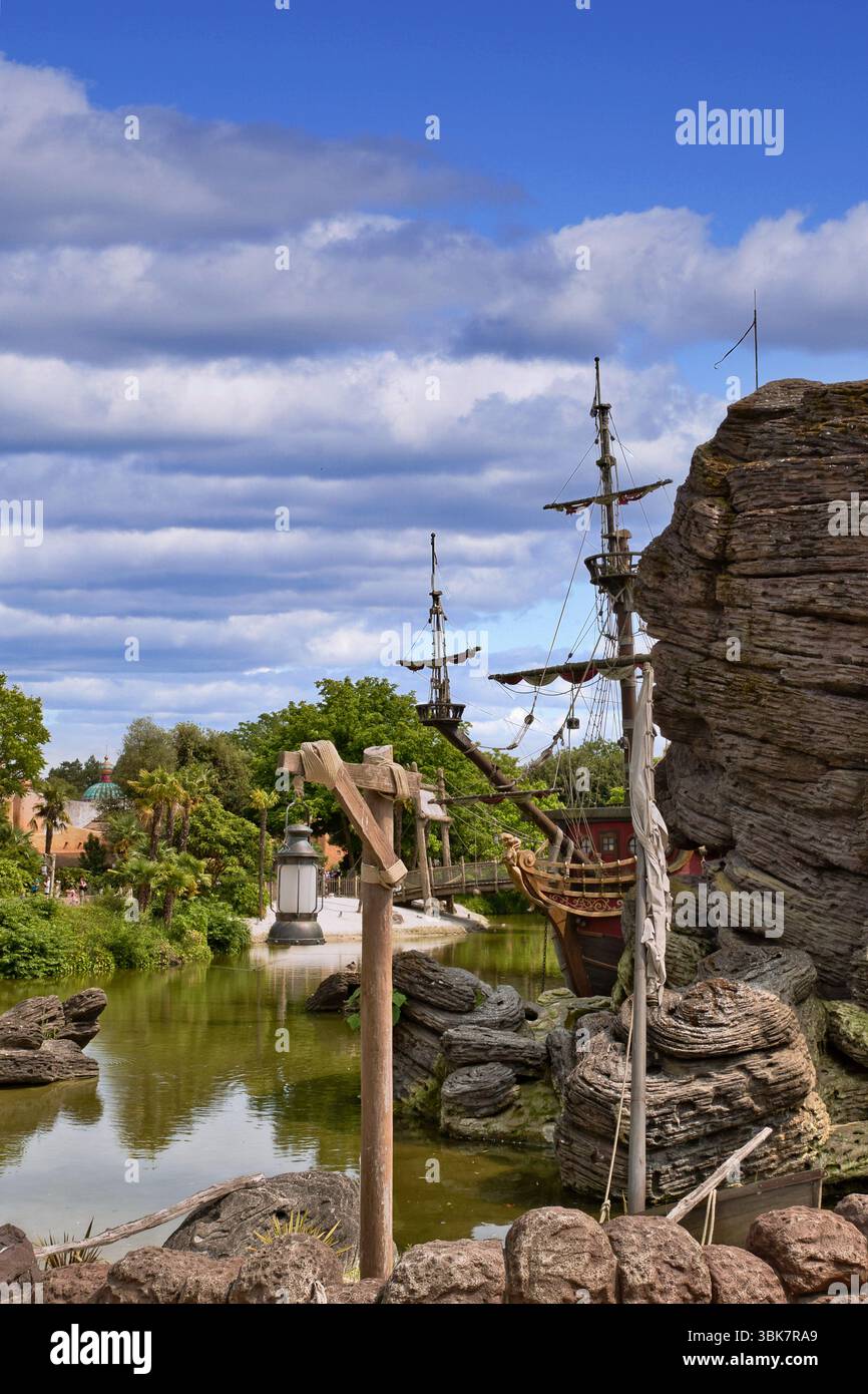 Scenic view of a pirate ship docked in a lagoon, surrounded by rocks, greenery, and a partly ...