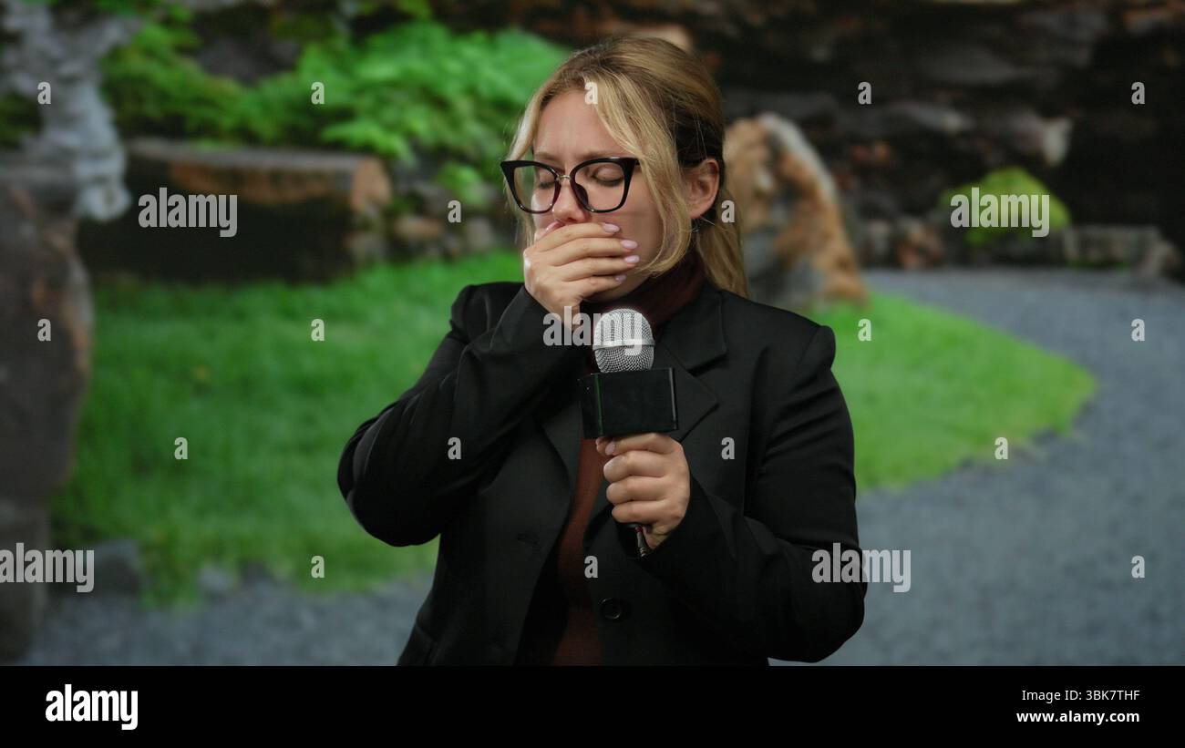 Woman reporter holding microphone appears emotional in an outdoor park setting with lush ...