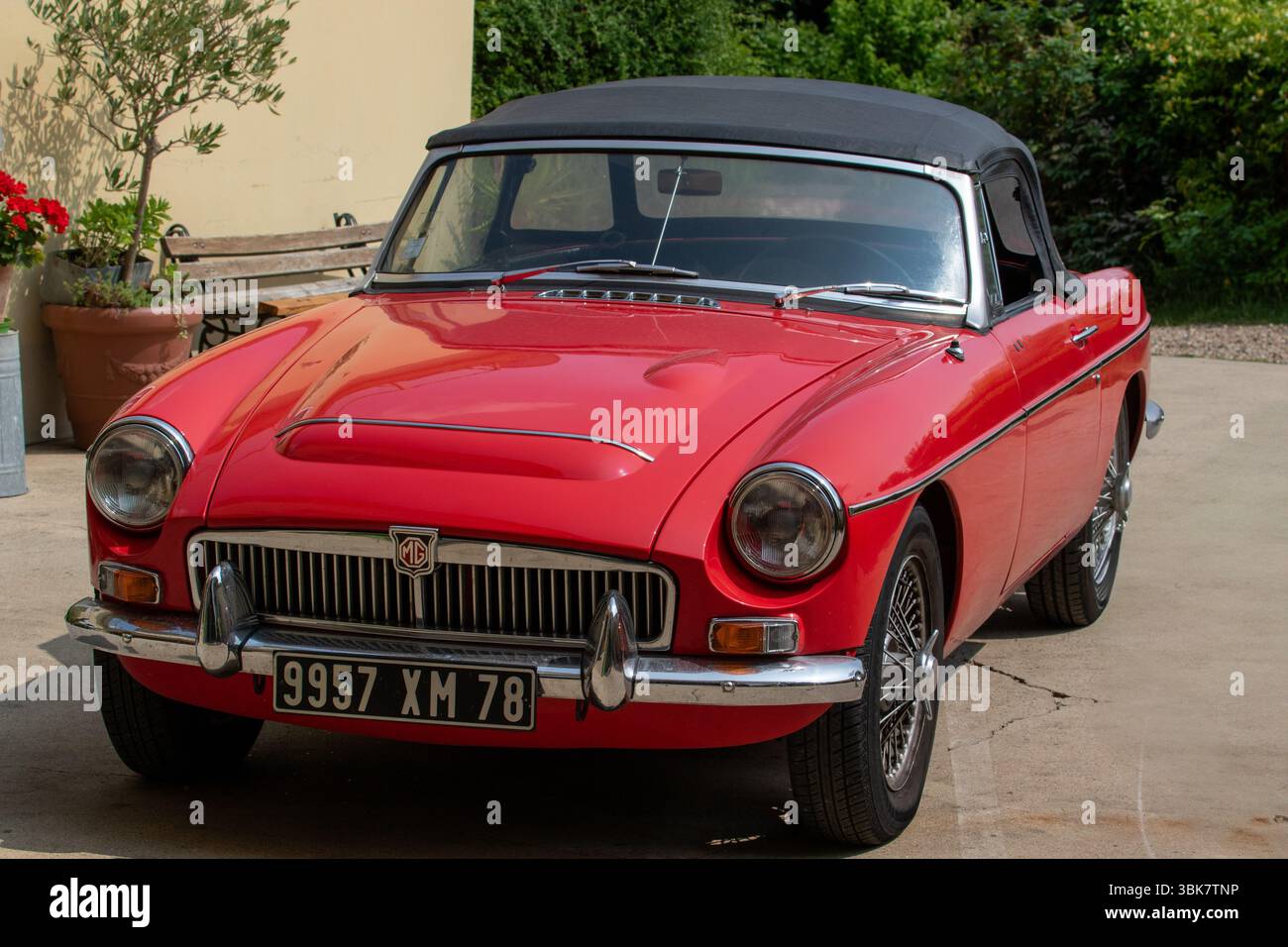 A bright red MG MGB convertible is parked on a concrete surface, facing ...