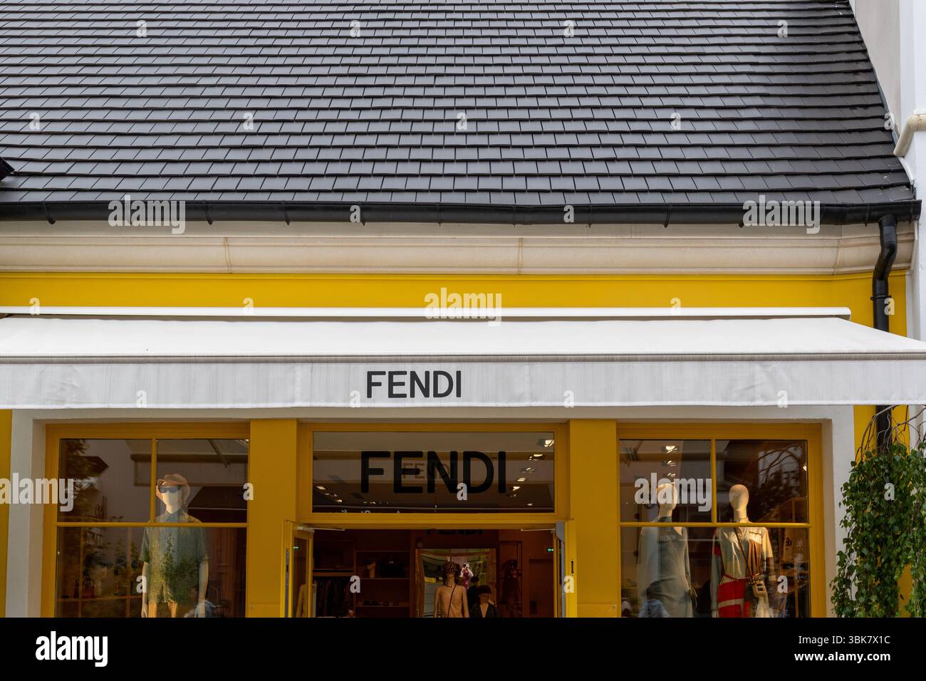 A bright yellow FENDI store front with black tile roof, awning, window ...