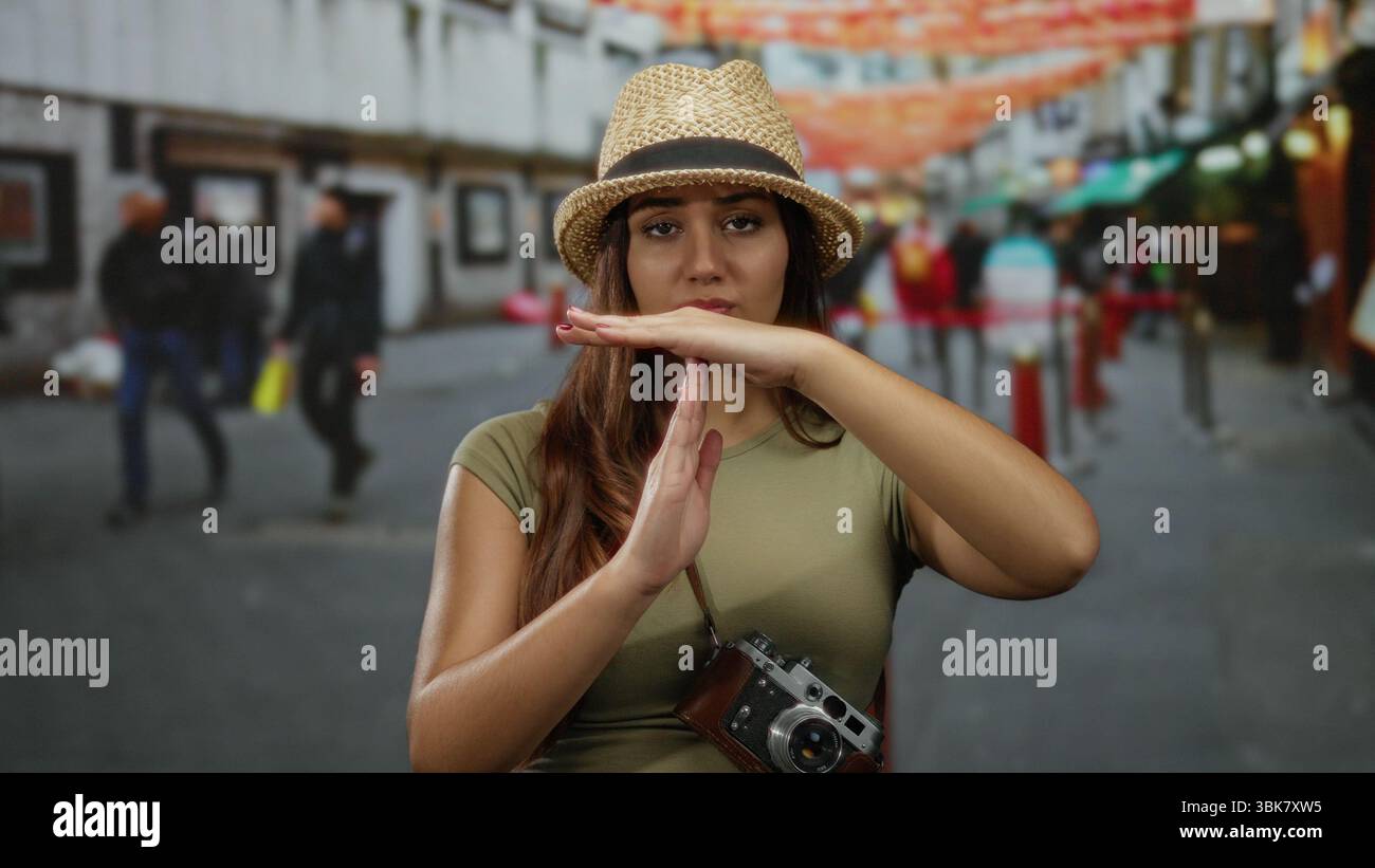 Hispanic woman wearing hat gestures timeout in busy outdoor street ...