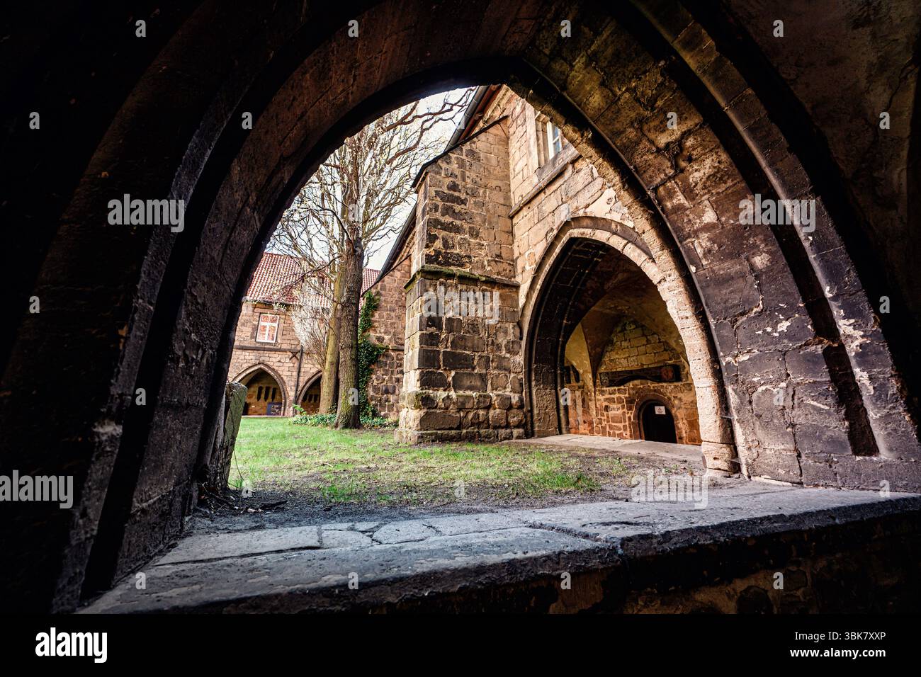 View through a dark stone arch reveals a grassy courtyard surrounded by ...