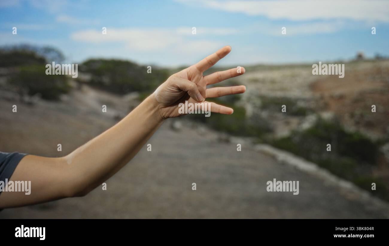 Hand of man showing four fingers against a blurred outdoor park ...