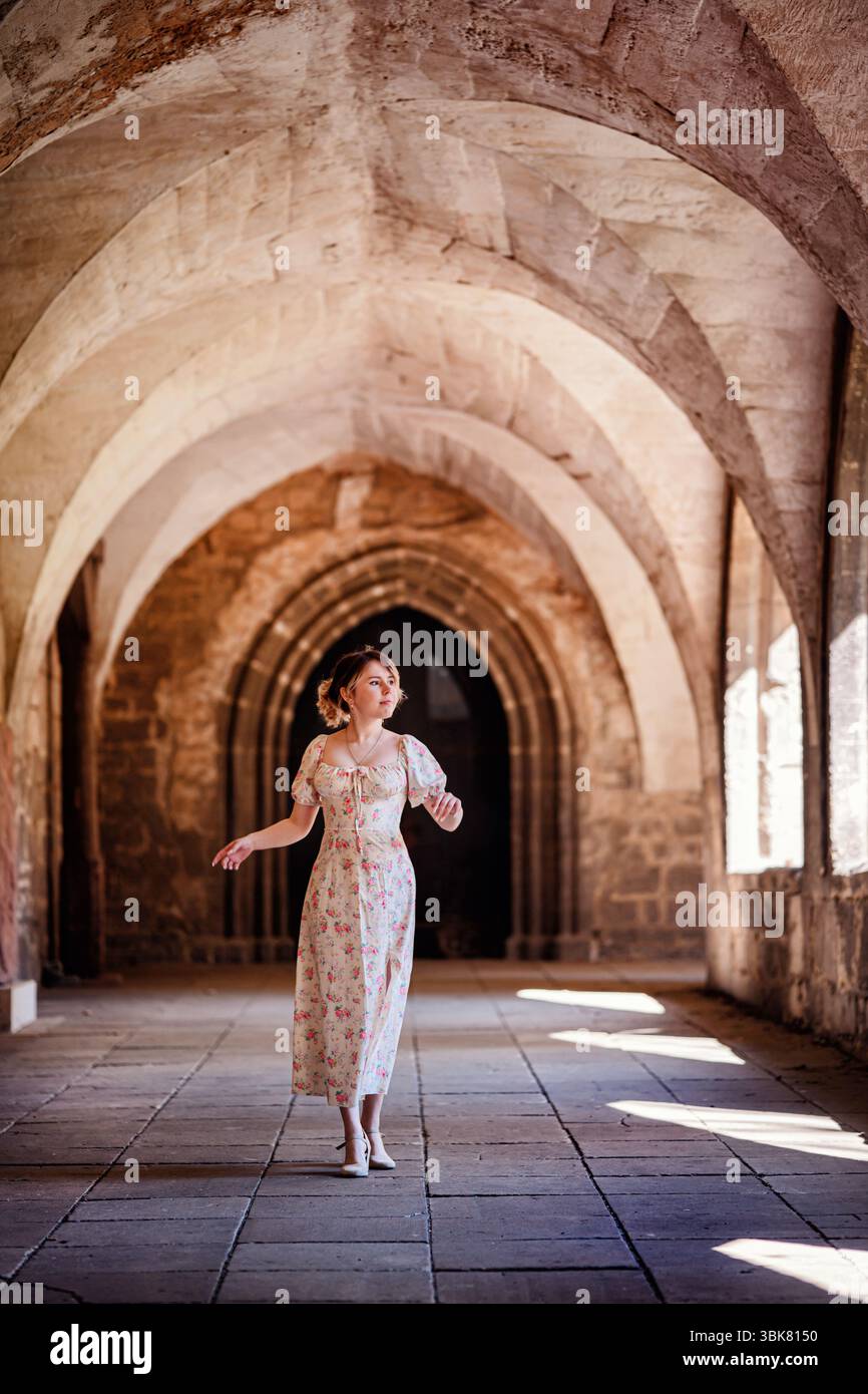 Young woman in a vintage floral dress walks under arched ceilings in a ...