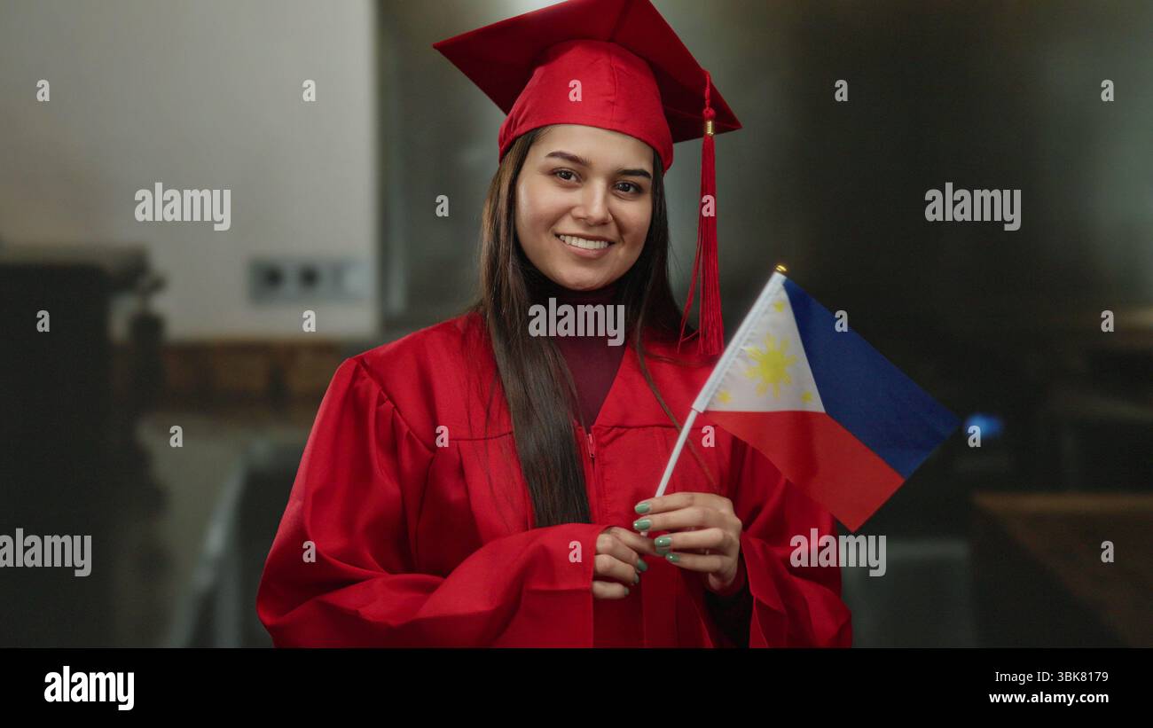 Young woman in a red graduation gown holding a philippines flag smiles ...
