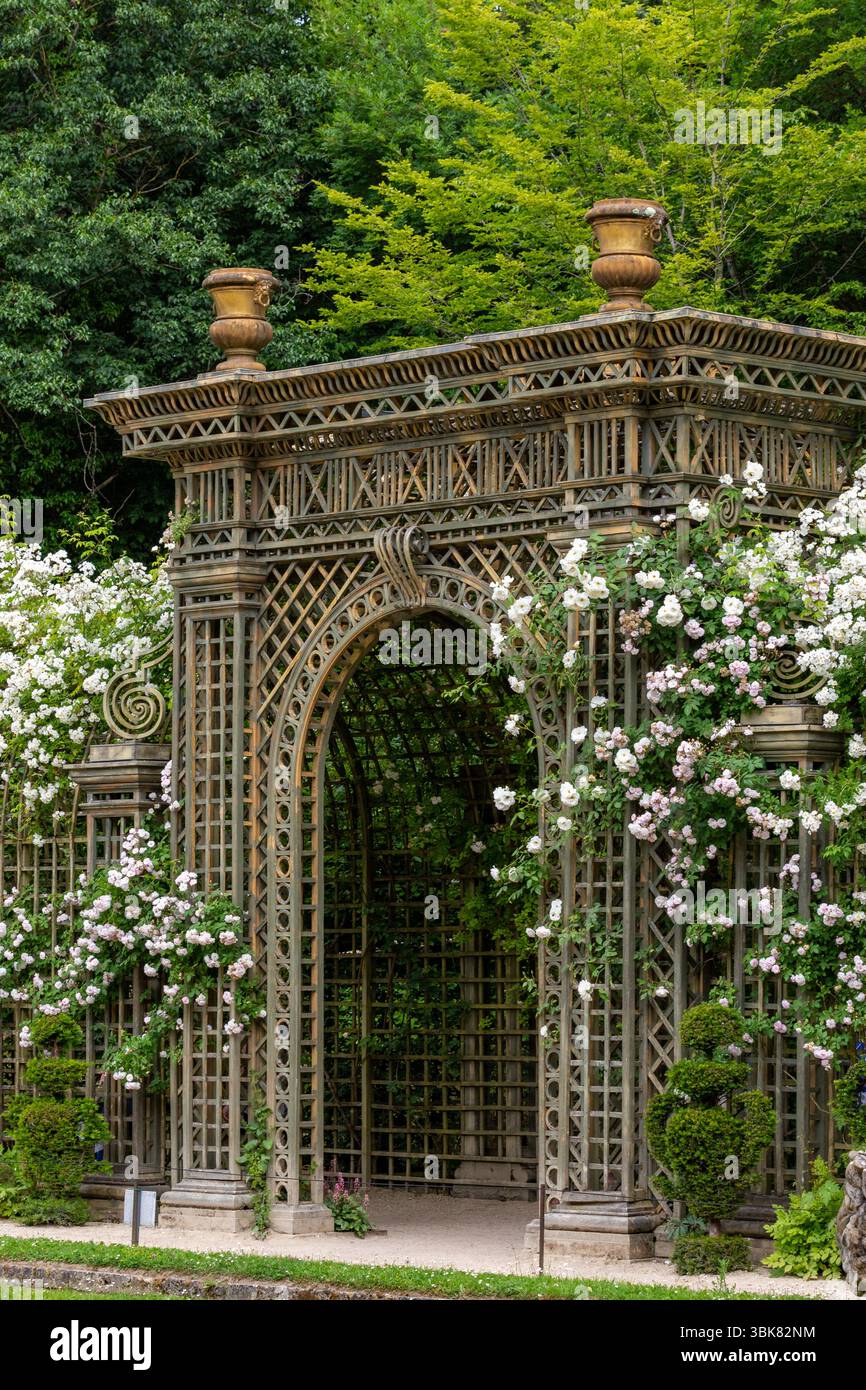 A garden archway structure, covered in climbing roses, sits within lush ...